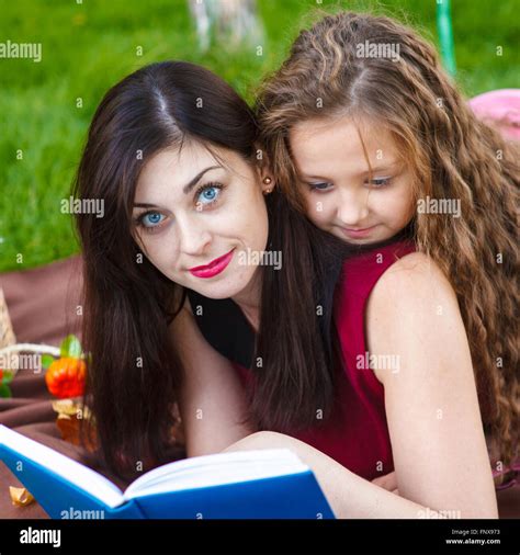 Mom And Daughter Reading A Book Lying On The Plaid In The Park Stock