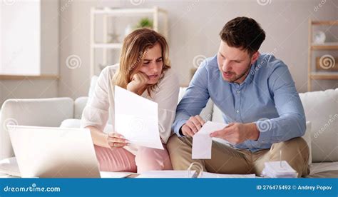 Shocked Young Couple Sitting On Sofa Looking At Bill Stock Image