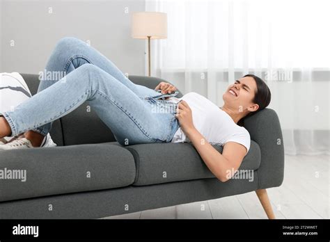 Young Woman Struggling To Squeeze Into Tight Jeans While Lying On Sofa
