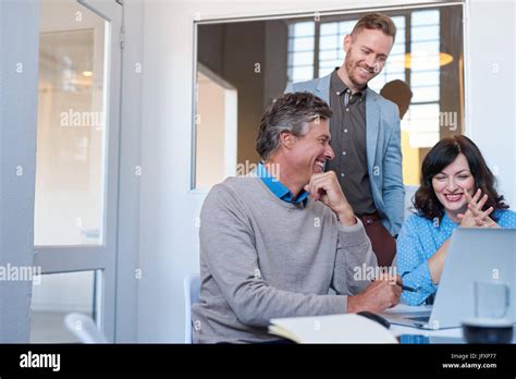 Smiling Office Coworkers Talking Together While Using A Laptop Stock