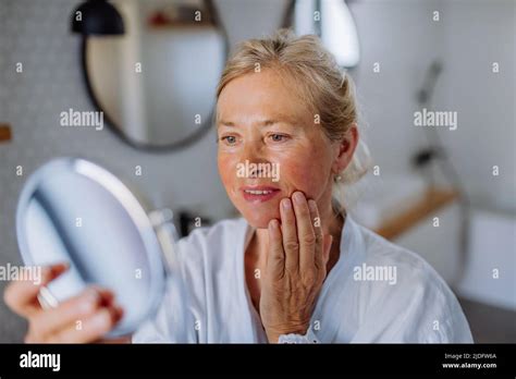 Beautiful Senior Woman In Bathrobe Looking At Mirror And Applying