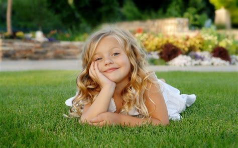 Blonde Haired Girl In White Dress Laying Down On Green Grass With Head