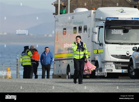 A Police Officer Walks Past An Irish Coastguard Vehicle With Flowers At