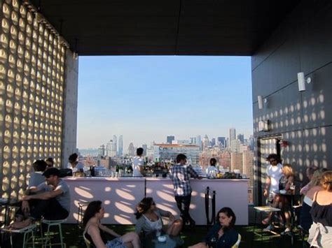 People Sitting And Standing On The Roof Of A Building With Cityscape In