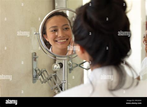 Happy Asian Woman Wearing Bathrobe Looking In Bathroom Mirror Touching