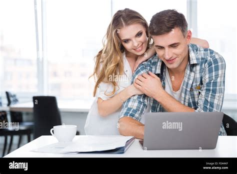 Happy Beautiful Couple Using Laptop Together Sitting At The Table At