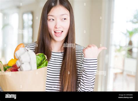 Beautiful Asian Woman Holding Paper Bag Of Fresh Groceries Pointing And