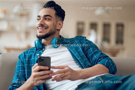 Young Man In A Blue Tshirt With A Phone In Hands Sitting On The Sofaの写真
