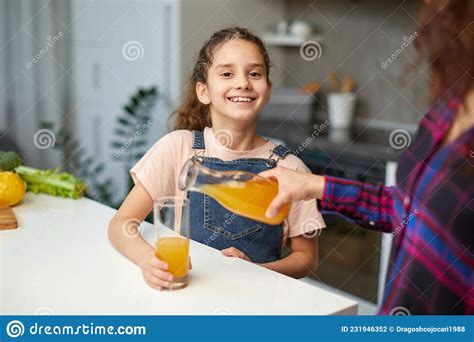 Portrait Of A Mom Pours Her Cute Daughter Orange Juice For Breakfast