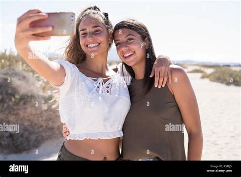 Girlfriends Having Fun On The Beach Taking Smartphone Selfies Stock