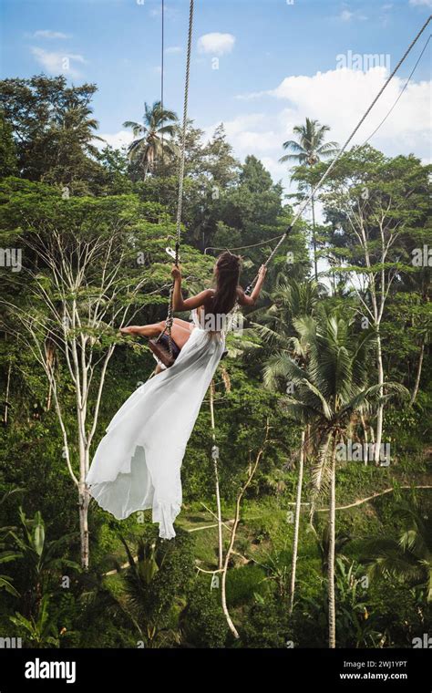 Woman Wearing White Dress Swinging On Rope Swings With Beautiful View