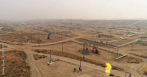 Gas flare coming out of a flare stack in California, vast oil fields with pipelines transporting oil from oil pumps, aerial drone shot