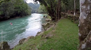 People float down a tropical river in tubes while a woman jumps off a rope swing at Semuc Champey, Guatemala