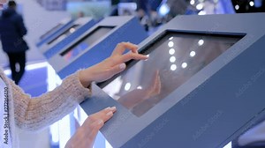 Woman using interactive touchscreen display of electronic multimedia kiosk at technology exhibition - scrolling and touching. Education, learning and technology concept