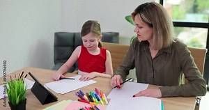 Teacher explains material to schoolgirl during home lesson in living room. Female tutor helps little student with homework printed on school paper