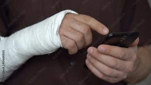 A man with a broken right hand in a plaster uses a smartphone to search for information. A fracture of the hand led to disability. Health insurance. Hands close-up