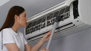 Young woman using vacuum cleaner to cleaning the air conditioner at home
