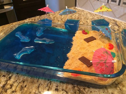 See how to make this gummy shark infested Jello treat. This dessert is made with blue raspberry Jello and filled with gummy sharks. The beach is made of crushed graham crackers. A fun dessert to make with the kids. Full Recipe: https://youtu.be/wsQzMFvcYKA | FunFoods