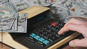 Counting on an old vintage calculator surrounded by dollar bills, close-up. Male hand press keyboard buttons on an old retro calculating machine. Counts finances, currency, savings, financial bills 4K