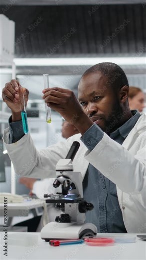 Vertical video Molecular biologist in lab analyzing batch of blood samples for red blood cell abnormalities. African american man doing research on sanguine fluid vials to diagnose anemia types