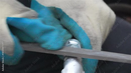 Metalworking filing workshop. Worker uses a rasp file tool to grind the sharp edges off a piece of metal tubing during industrial maintenance.
