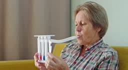 An elderly woman is engaged in a health exercise, blowing into a...