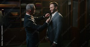 Cinematic shot of professional tailor taking measurements of client for creation custom tailored suit in a luxury tailoring atelier. Concept of fashion, handmade, hand craft, couturier and business.