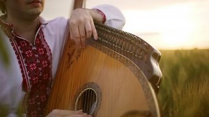 Young man playing pandora in wheat field at sunset. Close up.