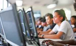 Digital Natives in the Making: A diverse group of students focused on computer screens in a modern classroom, highlighting the importance of technology in education.