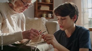 Starting knitting stitch lesson grandma guiding grandson's fingers on needles at home, with yarn