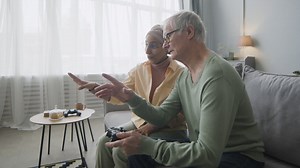 Free stock video - Middle aged arabic woman explaining to a senior man how to use the game controller while sitting together on couch at home 1
