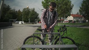 Man cyclist unlocks bicycle on bike parking lot outside in Germany. Male opens anti-theft padlock and takes cycle from street parking spot in Europe. Guy unlocking bicycle in open rack and leaves. 素材庫影片