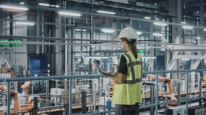 Female Car Factory Engineer in High Visibility Vest Using Laptop Computer. Automotive Industrial Manufacturing Facility Working on Vehicle Production with Robotic Technology. Automated Assembly Plant.