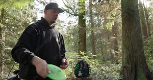 Medium shot of a man throwing a disc in the Pacific Northwest forest while playing disc golf
