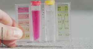 A hand holds a test tube with tests for PH and chlorine levels.
