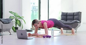 Fit woman does yoga plank pose on mat to strengthen body muscles. Female person enjoys online fitness via laptop repeating exercise after coach