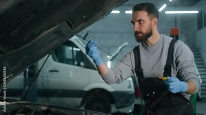 Car service station Caucasian man mechanic worker repairman open vehicle hood check engine oil fuel with dipstick tool adult male working with truck in garage transport maintenance automobile checkup