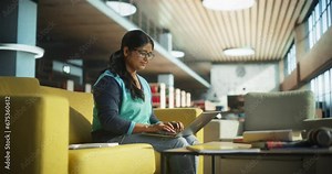 Focused Indian Female Working on a College Project for Class Assignment, Using Laptop Computer in a Public Library Space. Young South Asian Woman Learning New Skills Online while Doing Exercises