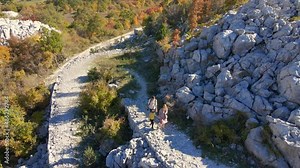 Aerial shot. Dron follows the family of a man woman and their son as they walk up the hill towards the Fortress Kosmach in Montenegro. An old fortress built by the Austrians as a defensive structure