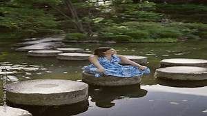 Beautiful hispanic woman sitting on a stone path, taking in nature's green summer splendor by a serene lake at heian jingu, kyoto - a divine journey, looking around traditional japanese temple