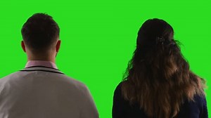 Close up studio rear view shot of male and female teachers or businesspeople facing away from camera towards green screen.