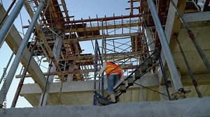 Female engineer climbing scaffolding to inspect work on upper floor of building, risk of work.