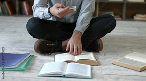 Midsection of male student with smart phone taking picture of books page and making cheat sheet for exam in college library. Man with mobile phone making screen shot of books page to cheat on his test