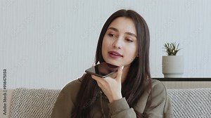 Young girl using voice recognition on phone to record message, sitting on couch at home