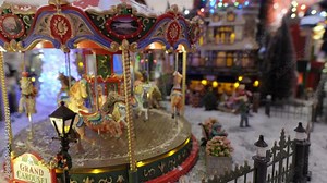 Closeup View of Christmas Village Miniature with Carousel with Moving Horses, lights, snow and christmas atmosphere.