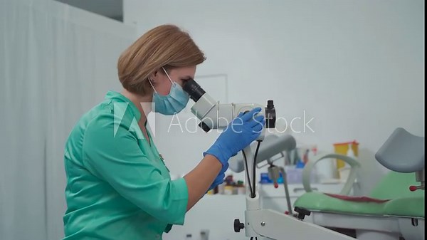 Gynecologist uses colposcope. Optical device with magnification designed for detailed examination of cervix, vagina, and vulva, aiding in diagnosing pathologies and detecting precancerous changes.