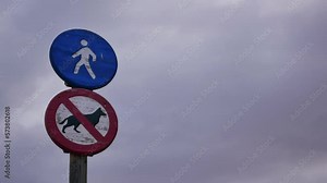 Timelapse and zoom in showing a pedestrian sign and no dogs sign. Grey cloudy sky.