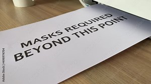 Printing “MASKS REQUIRED BEYOND THIS POINT” text written message on paper sheet A4 document. Close up page being printed from multifunction printer scanner in office. Hand take paper from printer