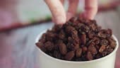 Fingers taking bunch of raisins from bowl on wooden table , dried...