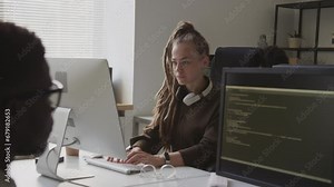 Waist up shot of young Caucasian female programmer with dreadlocks typing program code on wireless keyboard while working with diverse colleagues in open space office